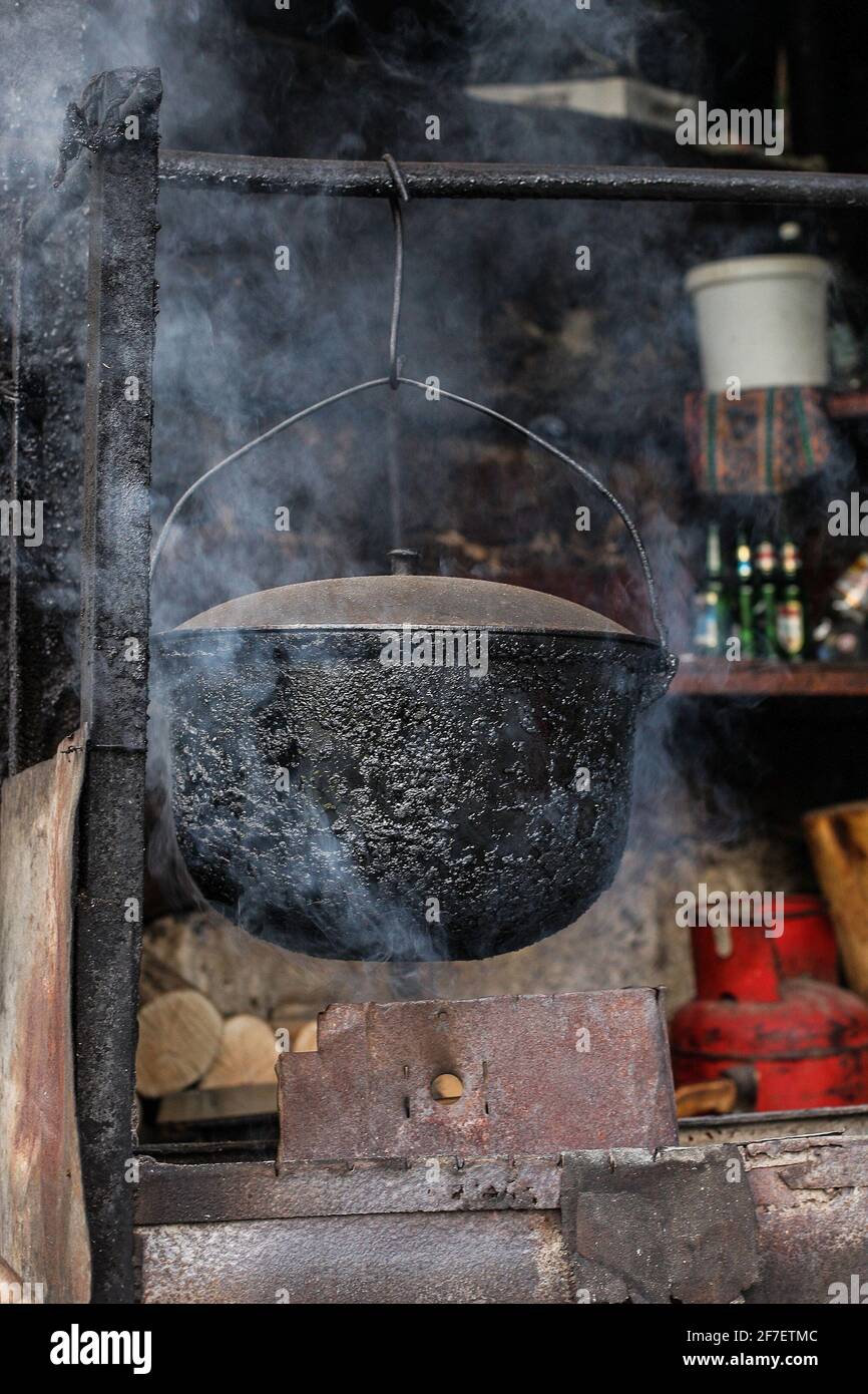 A stew or a soup is being prepared in a bowl above an open fire. Smoke ...