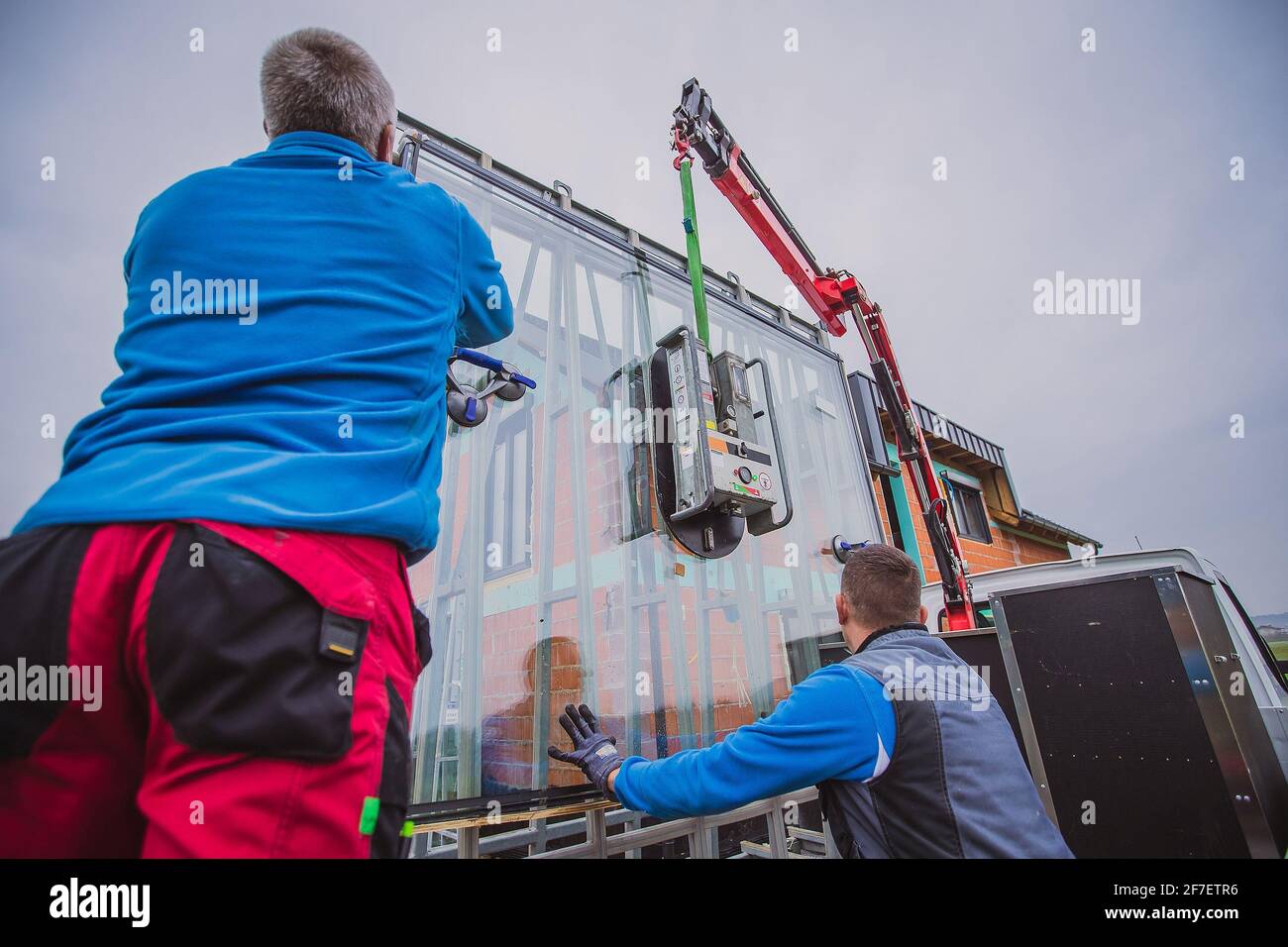 Two male workers lifting a big glass window or piece of glass from a ...