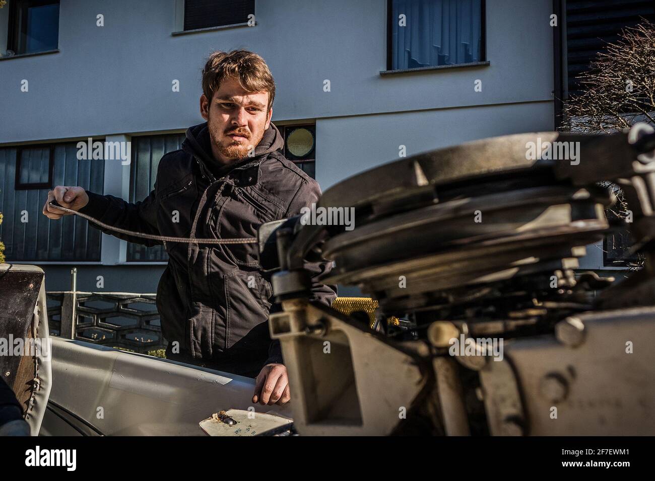 A young male is trying to start an outboard engine with pulling the ...