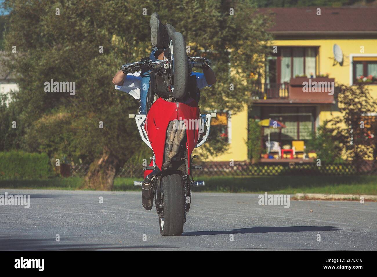 Motorcycle stunt man practicing on a home parking lot on a red and ...