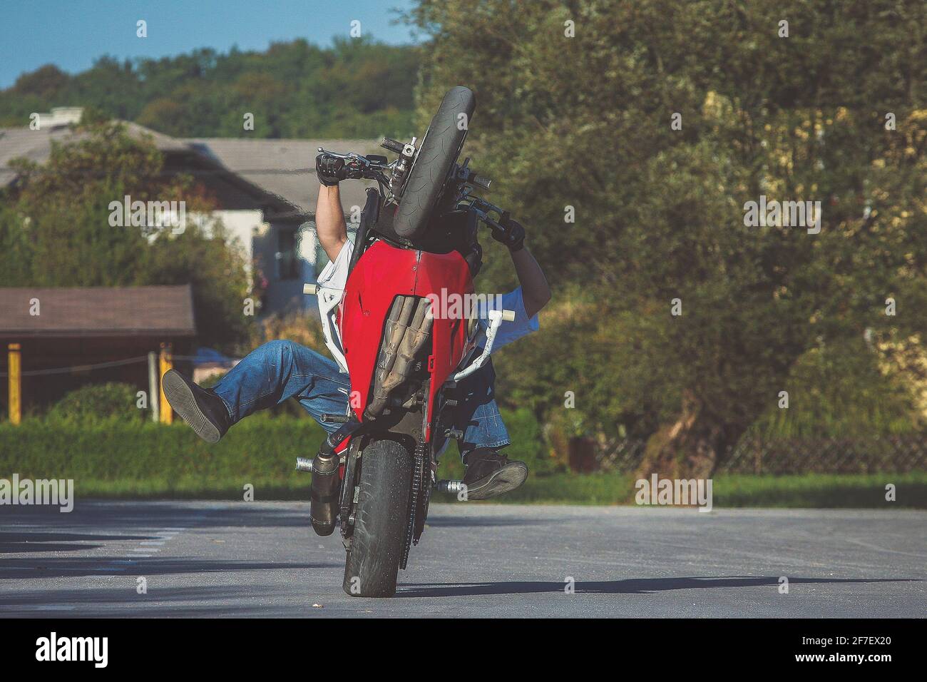 Motorcycle stunt man practicing on a home parking lot on a red and ...
