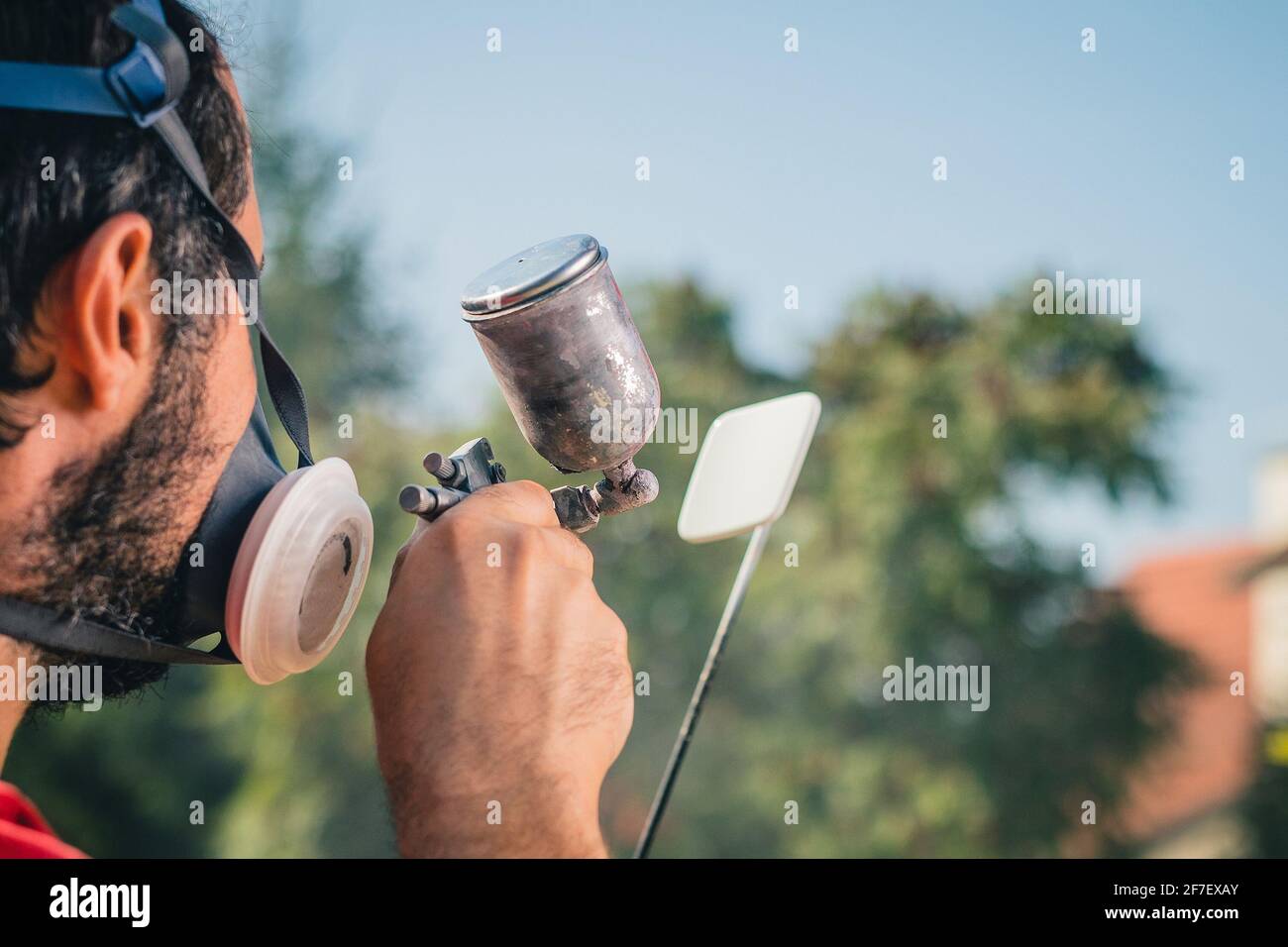 Amateur painter in red sweater and face mask using a spray gun to paint ...