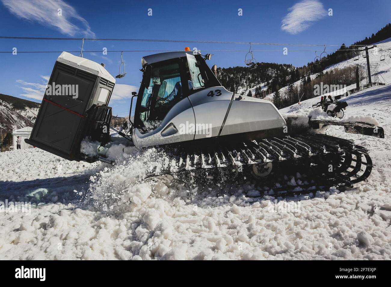 Snow grooming machine on a ski slope during midday, carrying a portable ...