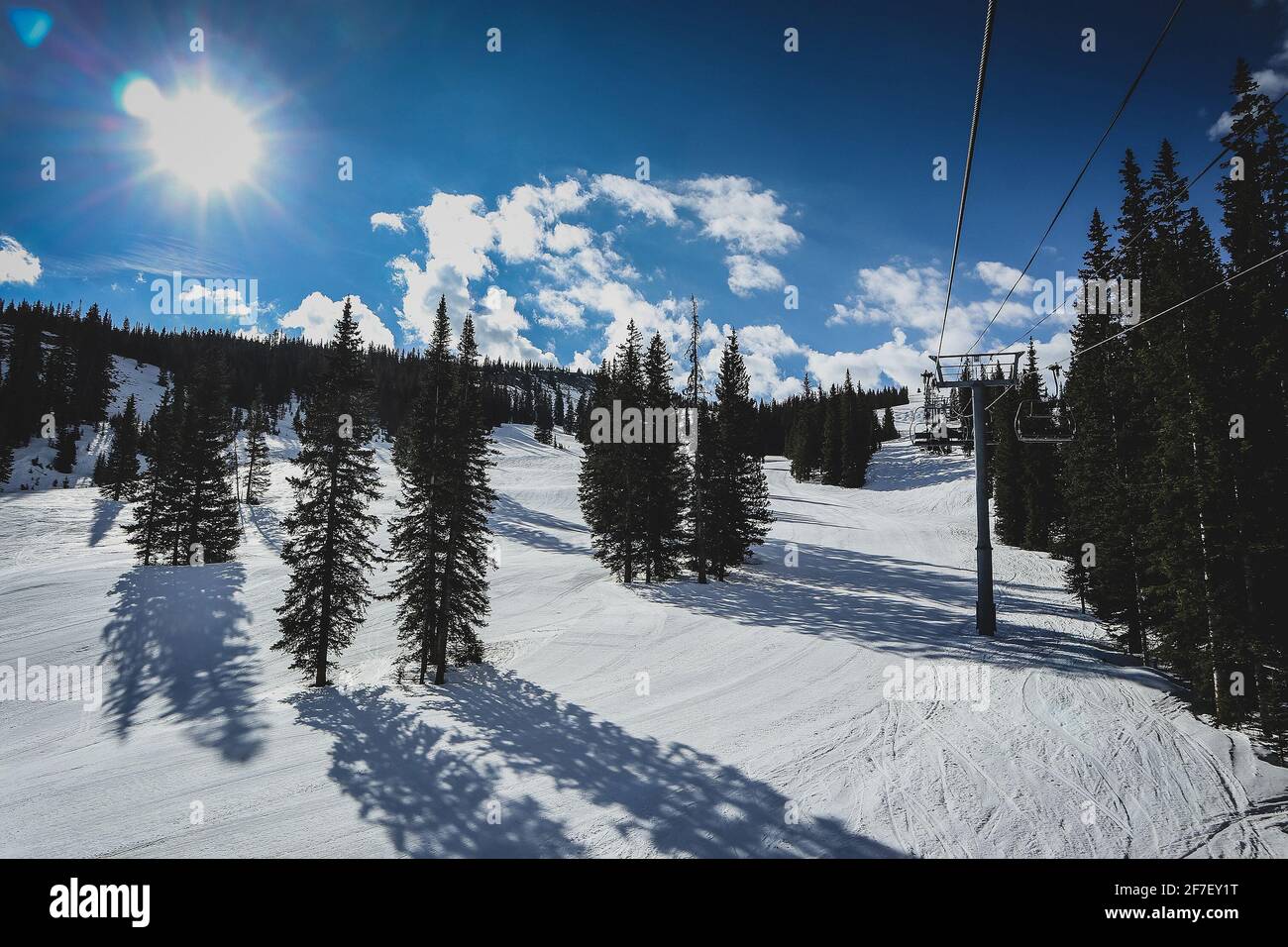Chair lift in Aspen in a sunny weather. Sun flare, trees and some ...