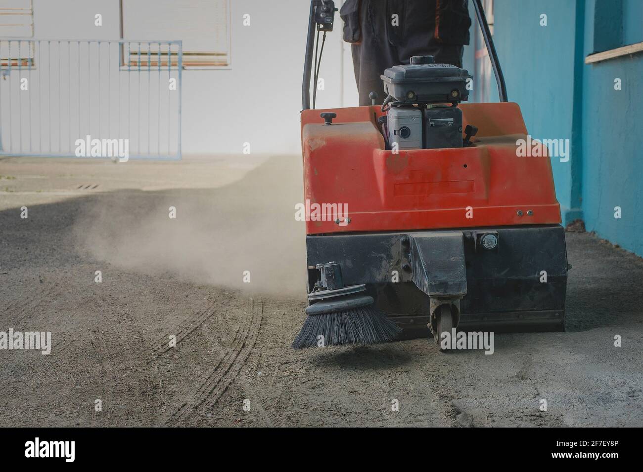 A person is pushing an orange gasoline powered industrial sweeper over ...