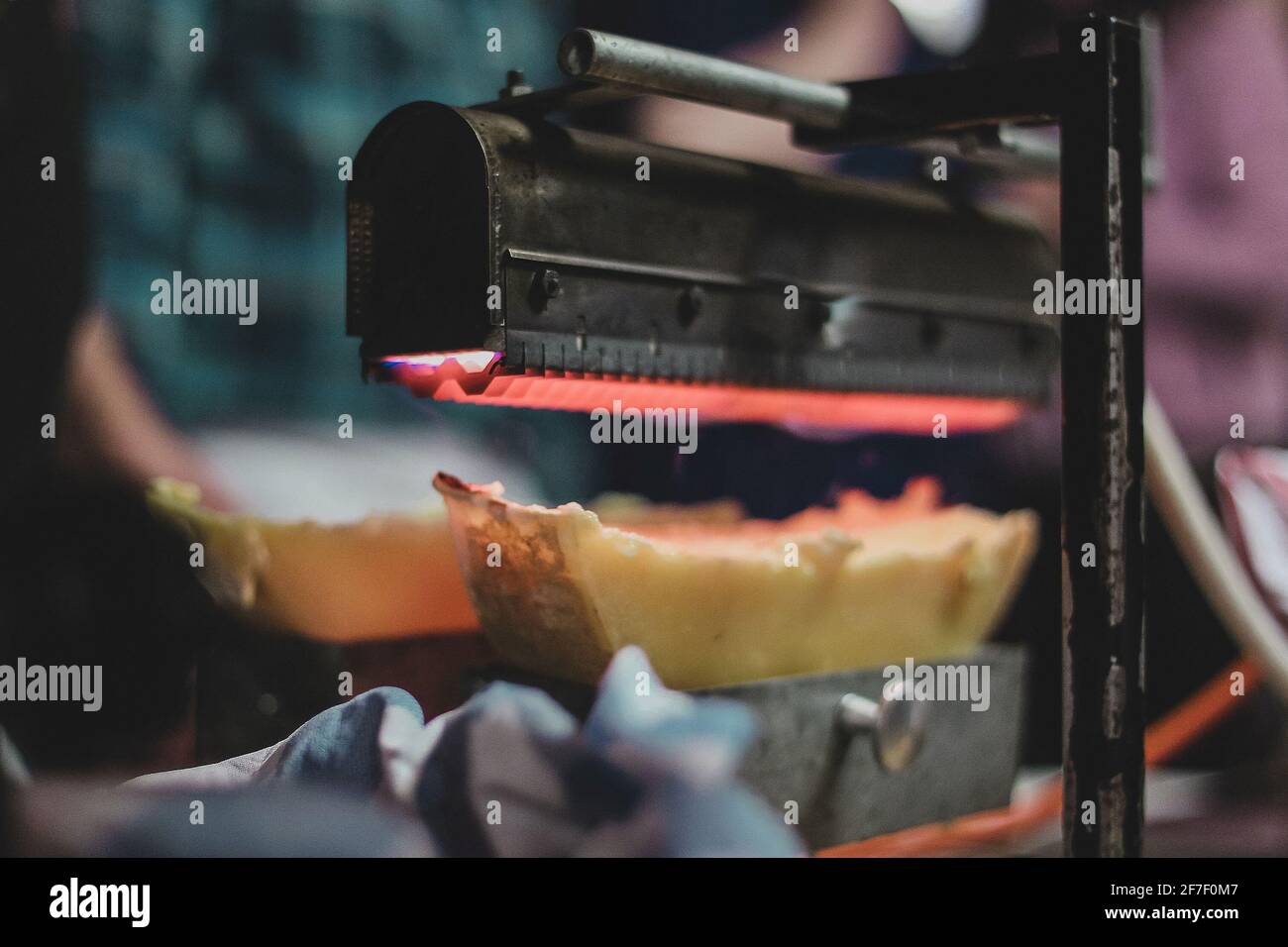 Detail of a raclette heater. Gourmet food being prepared under a gas ...