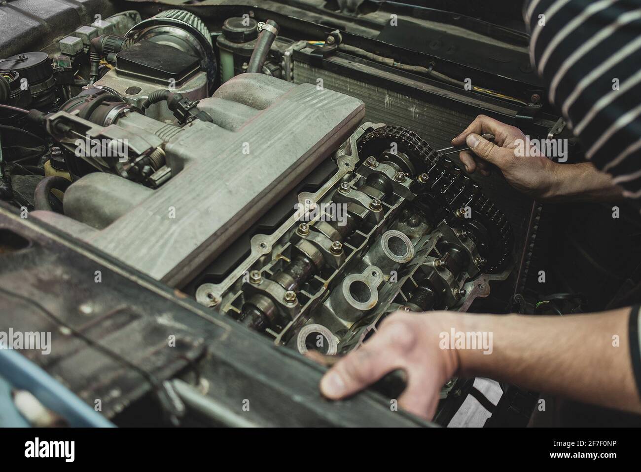 Young man fixing an engine of a car, using a wrench and looking into ...