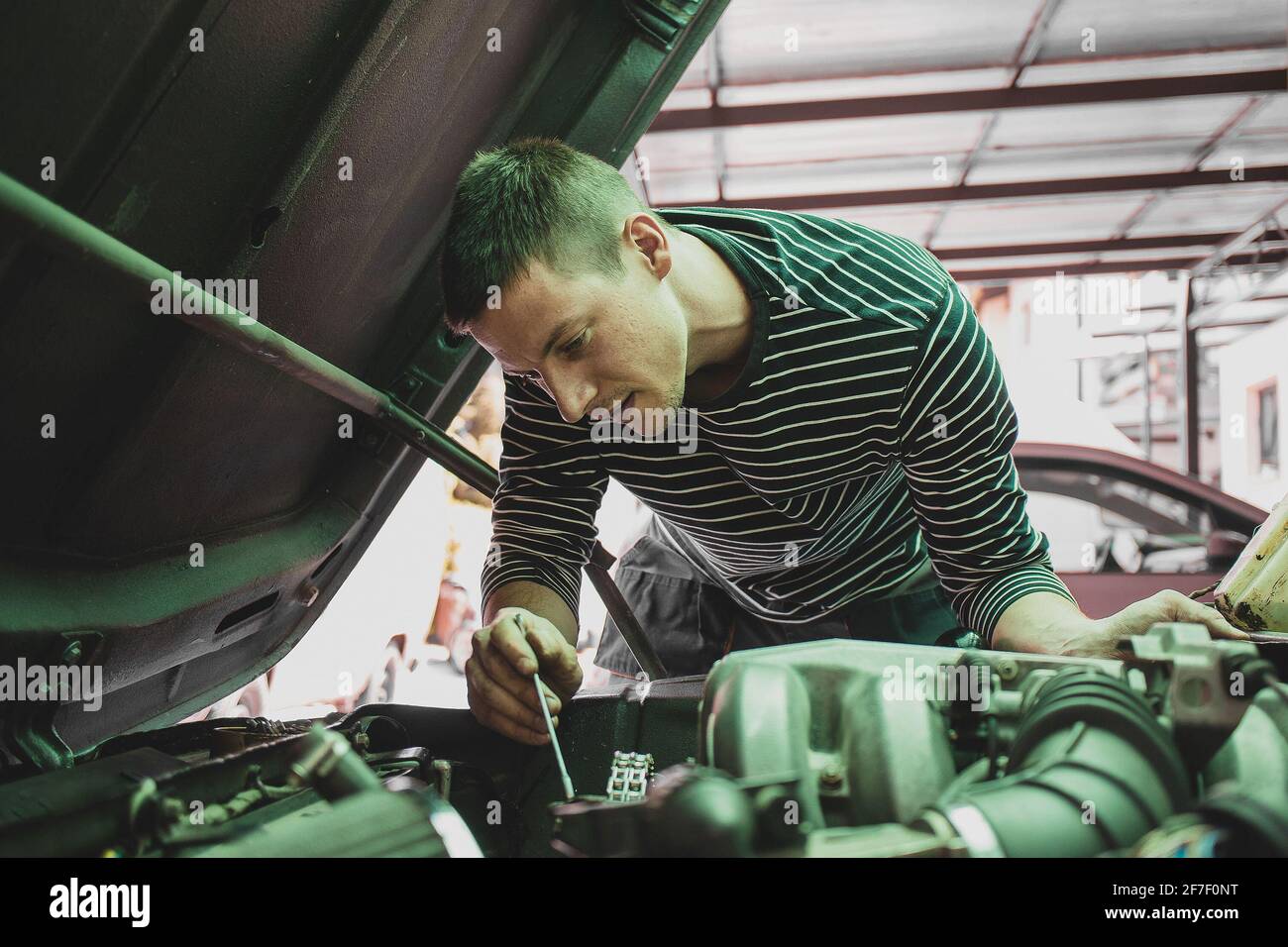 Young man fixing an engine of a car, using a wrench and looking into ...
