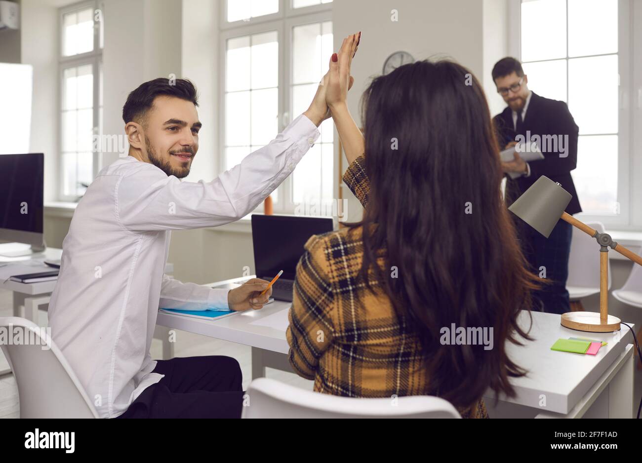 Two happy young people give high-five to each other sitting at table in ...