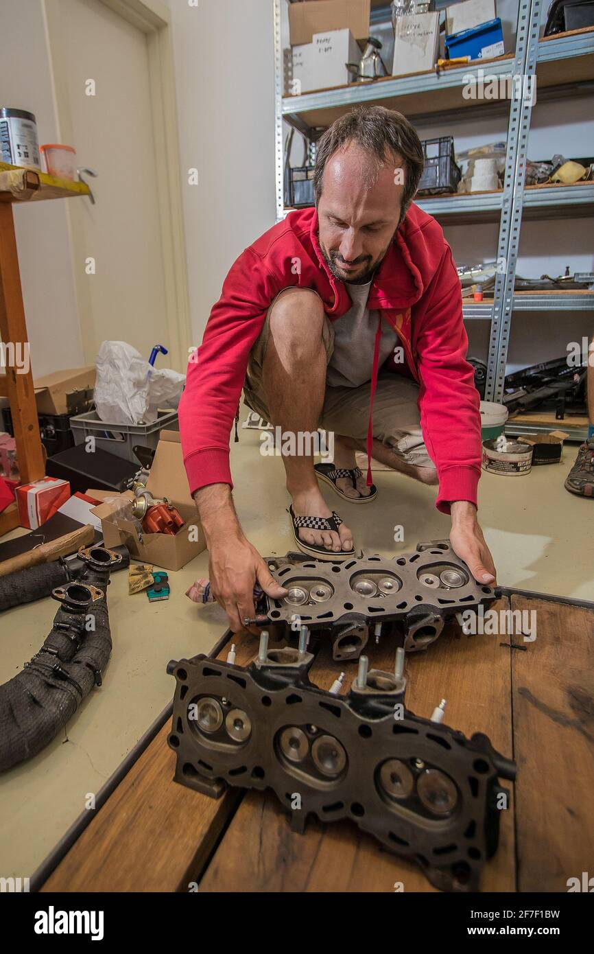 A home mechanic assembling a V6 cylinder heads on the floor of a garage ...