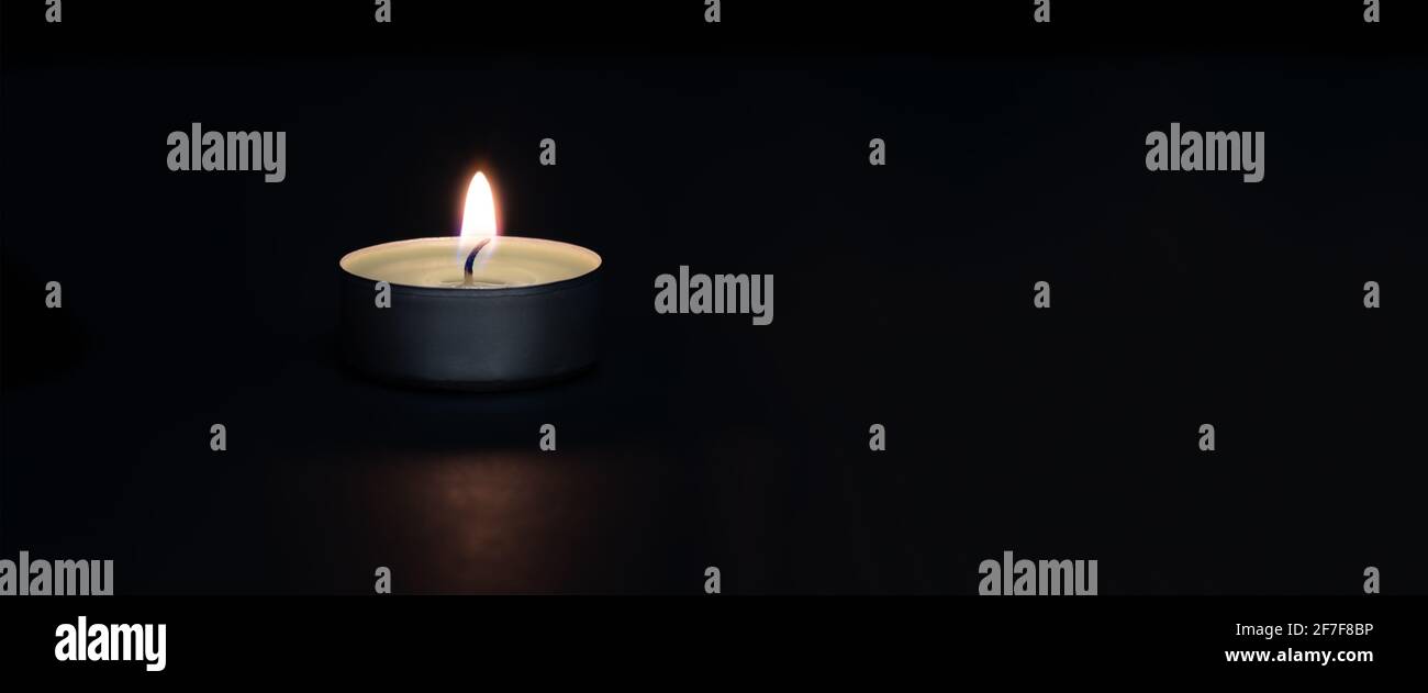 A burning candle on a dark background with a flare in the foreground ...