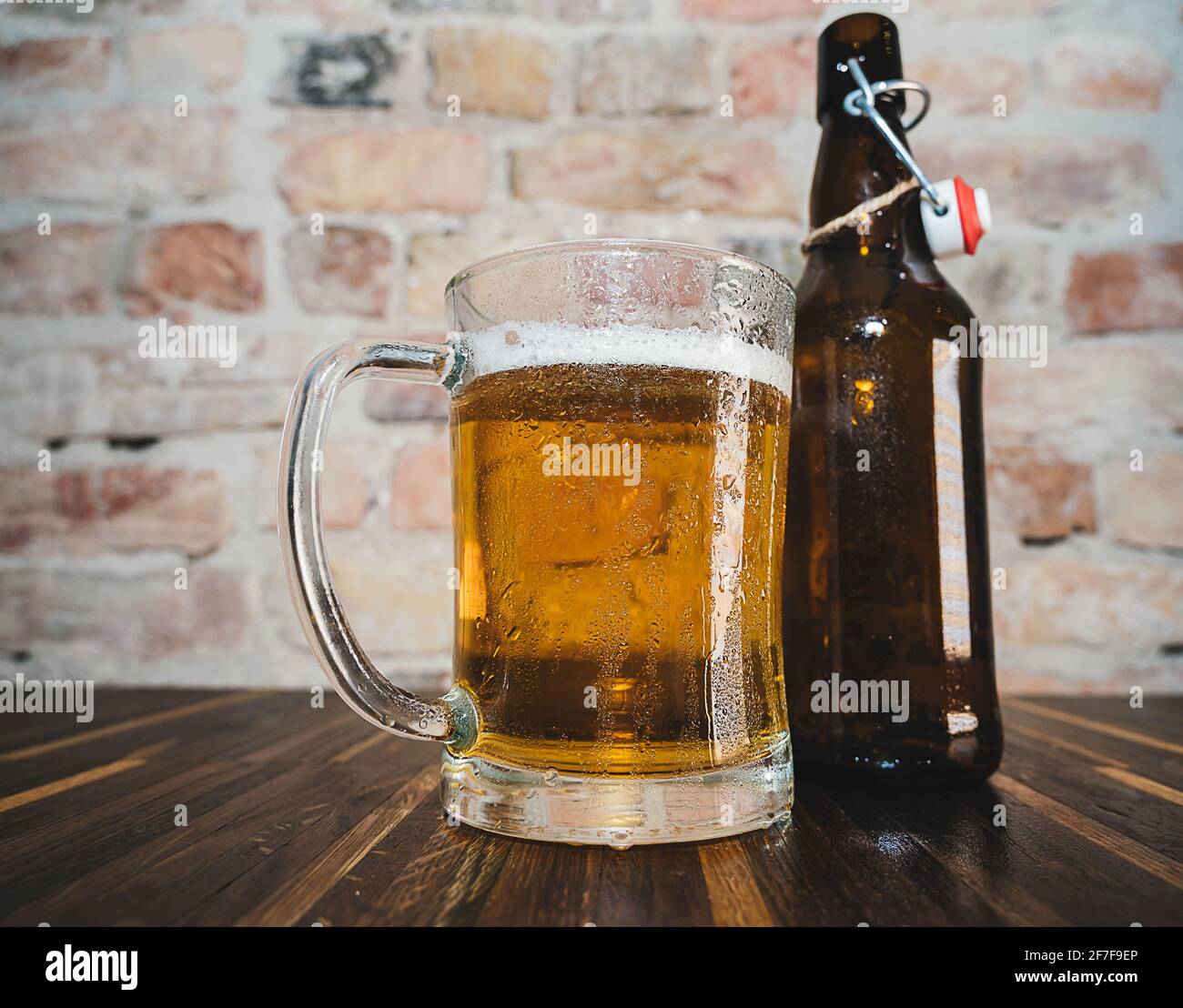 Glass pint with water drops and bottle of beer on wood table isolated ...