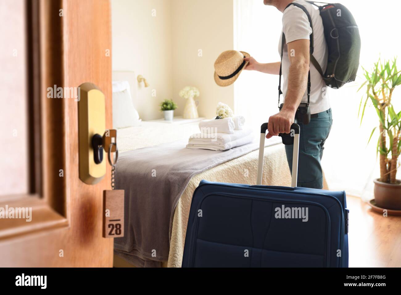 Man on vacation entering a bright hotel room with open door and key set ...