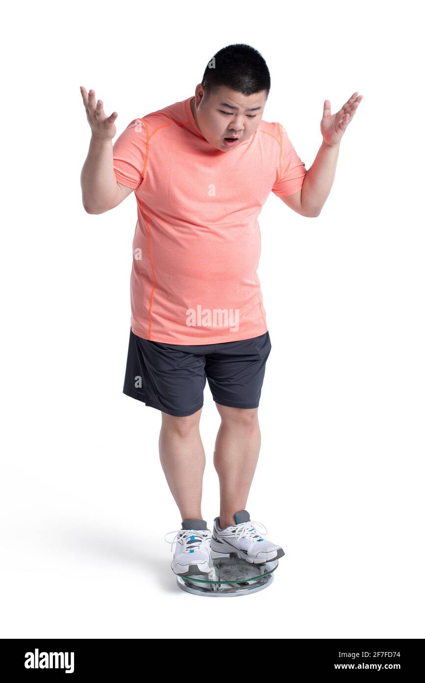 Overweight young man weighing himself on a scale Stock Photo - Alamy