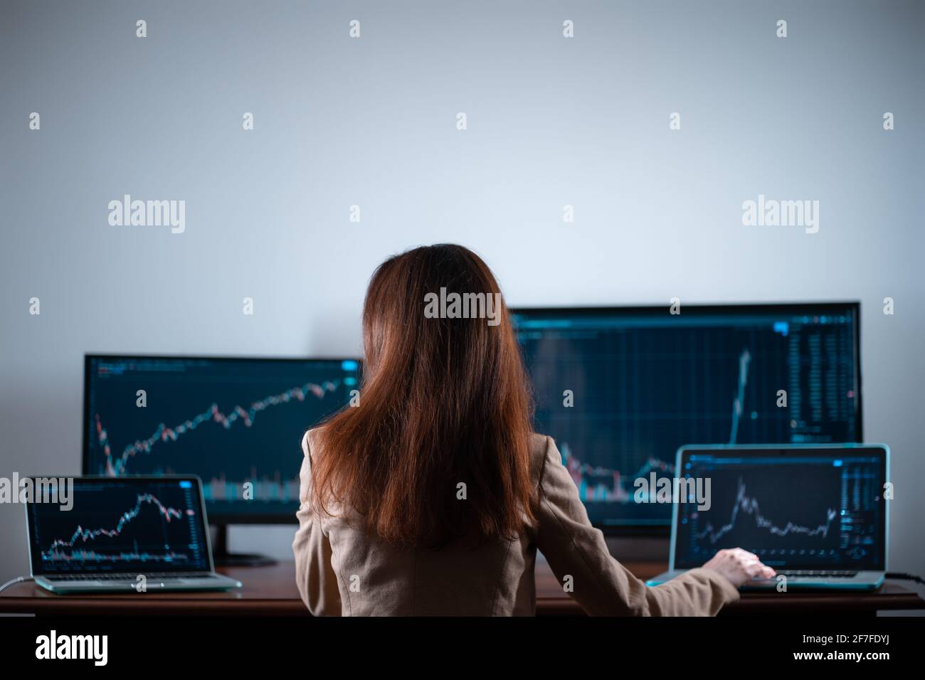 back view of female trader looking at monitor with stock exchange graph ...
