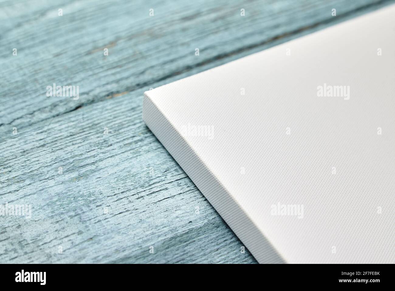 White canvas hanging on light blue wooden wall. Corner of blank canvas ...