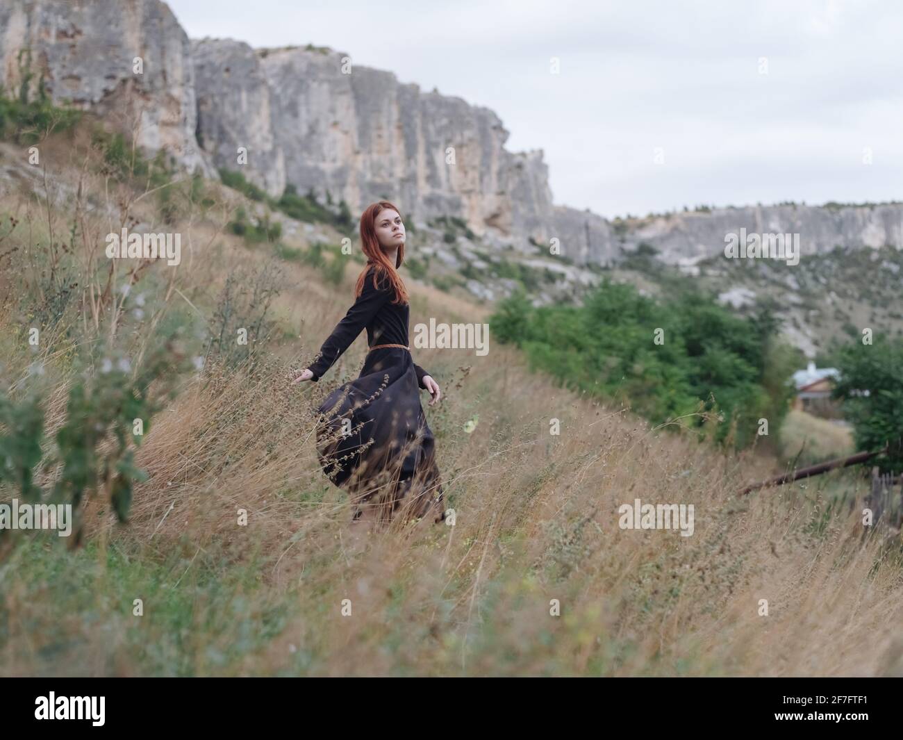 woman traveler in a black dress runs on dry grass in the meadow and ...
