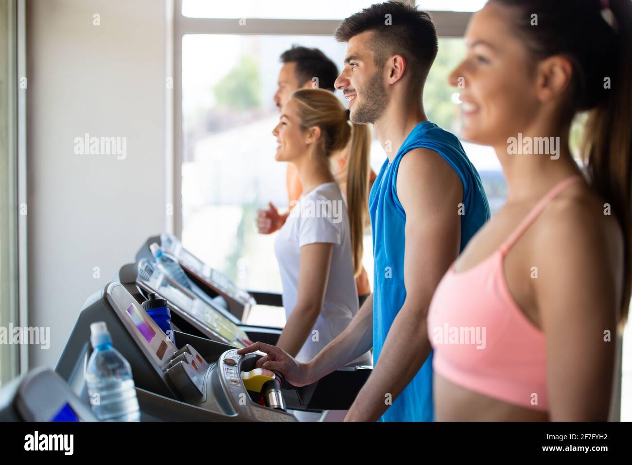 Group of happy fit young people running on a treadmill in health club ...