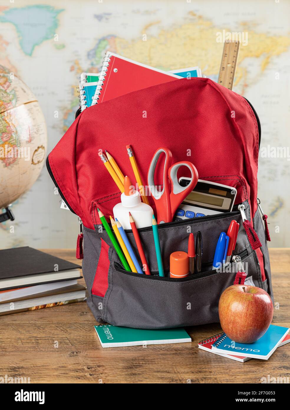 Book bag with an assortment of school supplies on a desk with world map ...