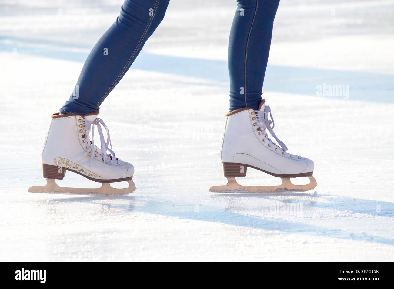 legs of a girl in blue jeans and white skates on an ice rink. hobbies ...