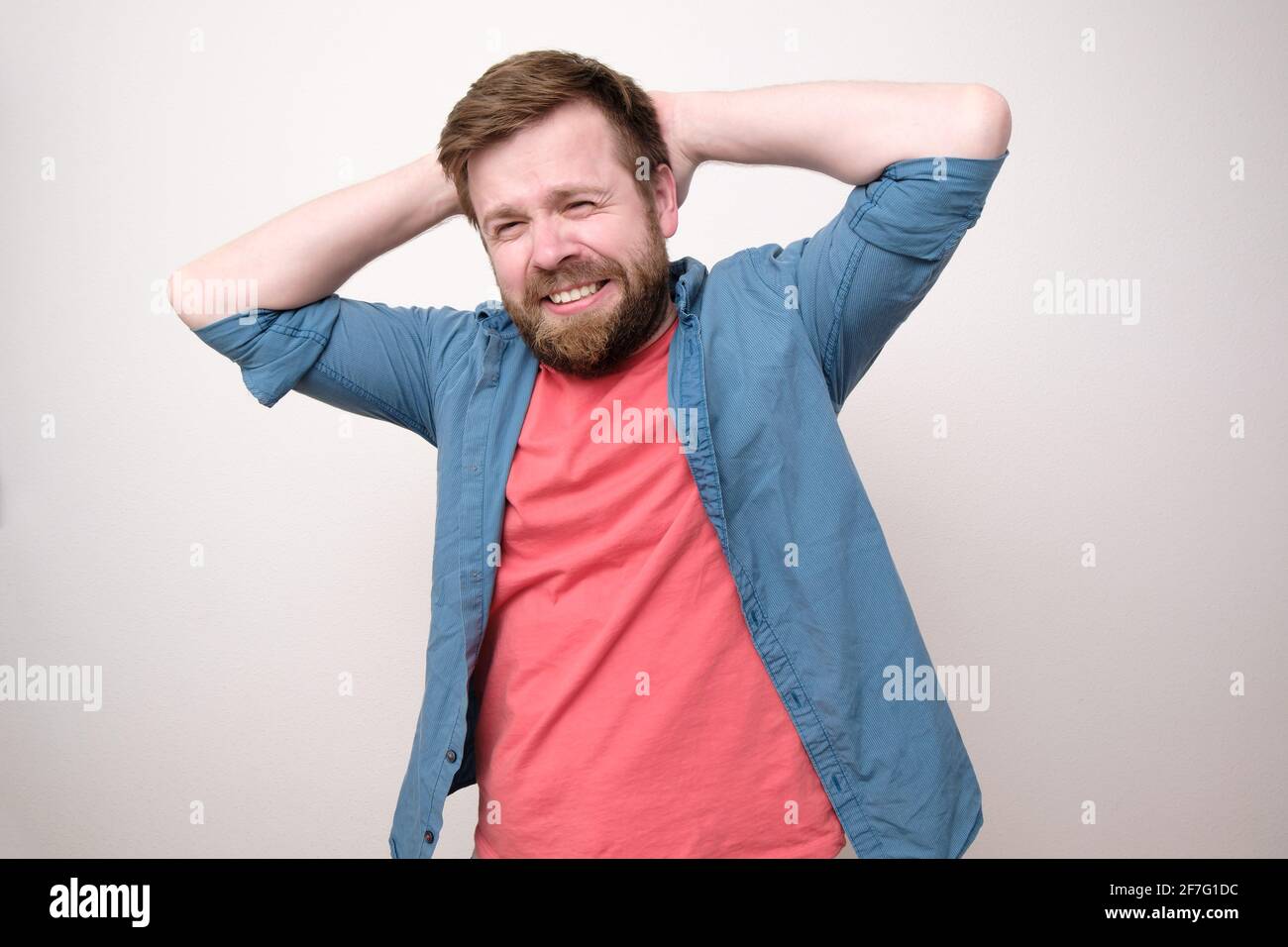 Shy, uncertain man smiles modestly with hands behind head. White ...