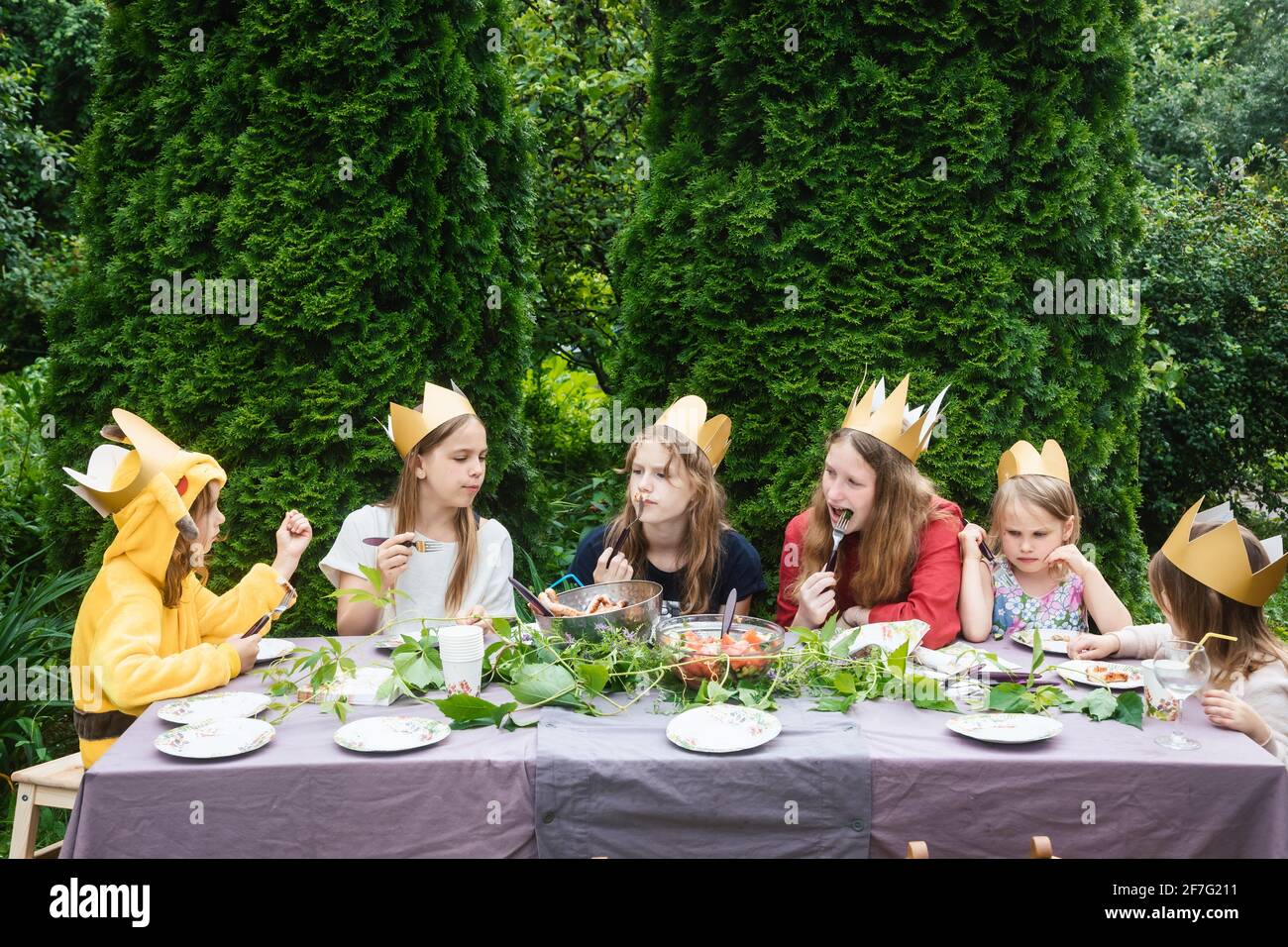 Children wearng paper crowns sitting by decorated table eating grilled ...