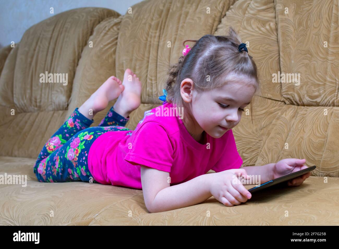 Little Girl Lying On A Comfortable Sofa Enjoying An Online Game On A