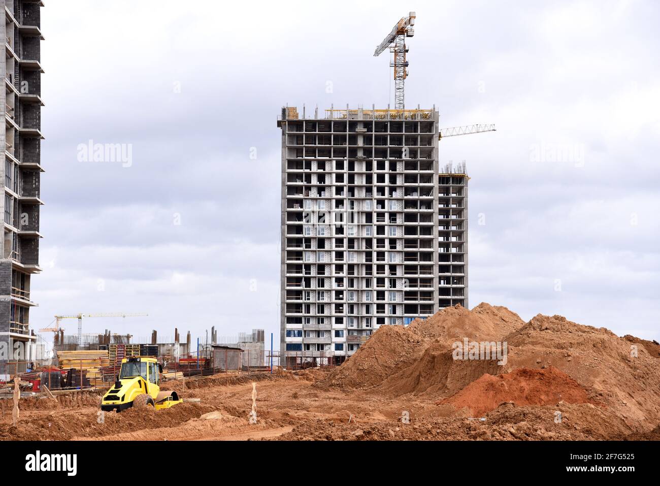View of the larger construction site. A soil compactor compacts the ...