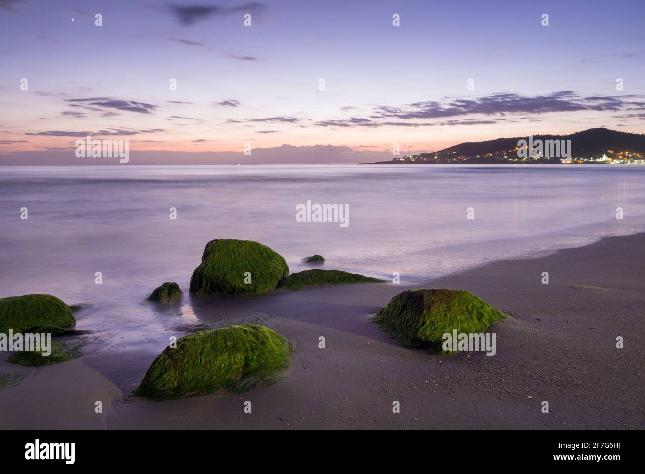 Beach sunrise with some green rocks in the foreground Stock Photo - Alamy