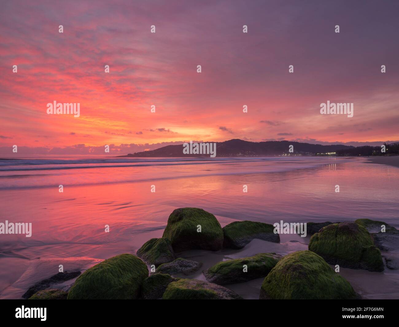 Beach sunrise with red sky reflected and green rocks Stock Photo - Alamy