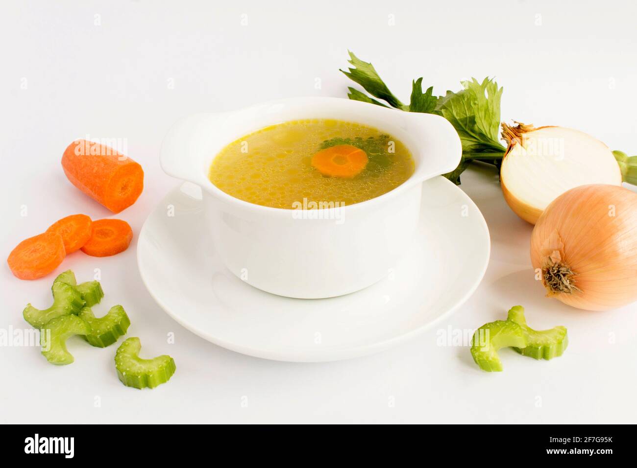 Chicken broth in the white bowl and vegetables on the light background ...