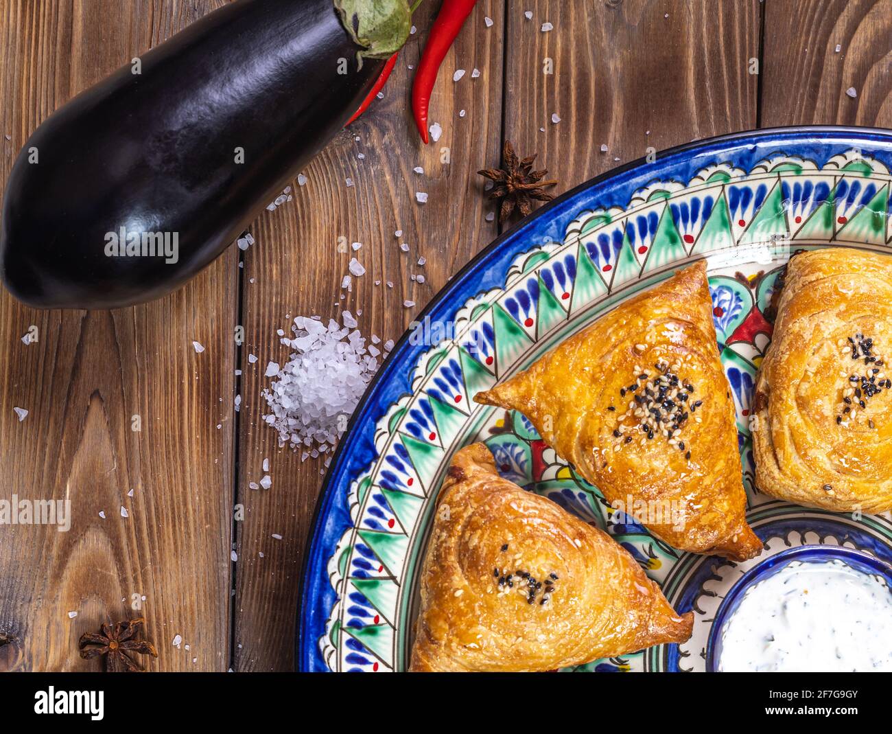 Samsa lies on a platter on a brown wooden background. Fresh baked goods ...