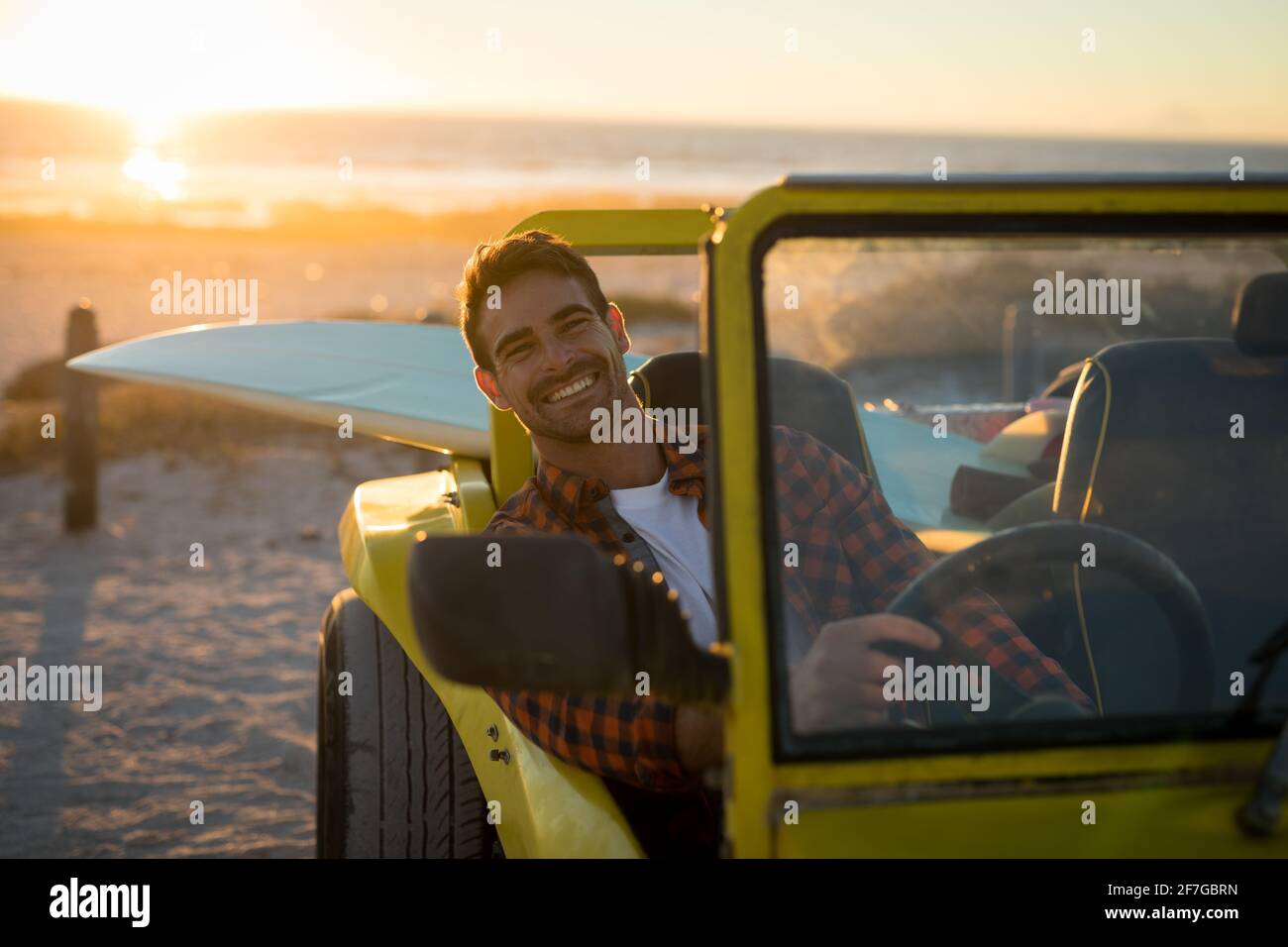 Happy caucasian man sitting in beach buggy by the sea during sunset ...