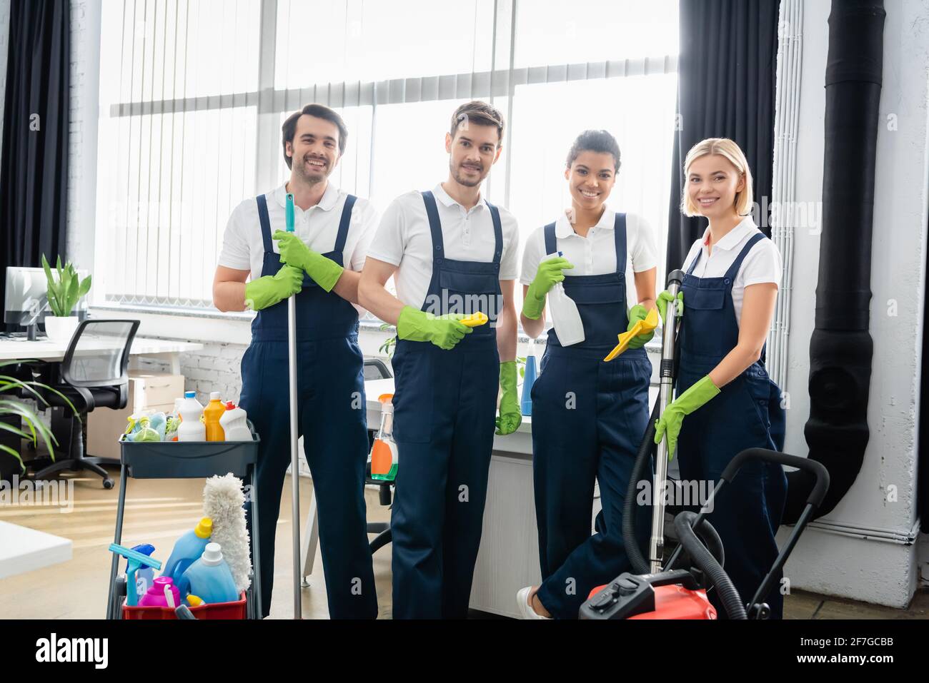 Multiethnic cleaners in uniform holding supplies in office Stock Photo ...