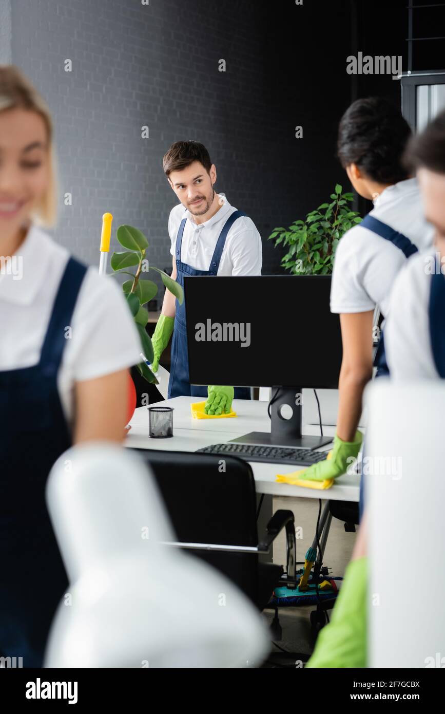 Cleaner looking at african american colleague cleaning table in office ...