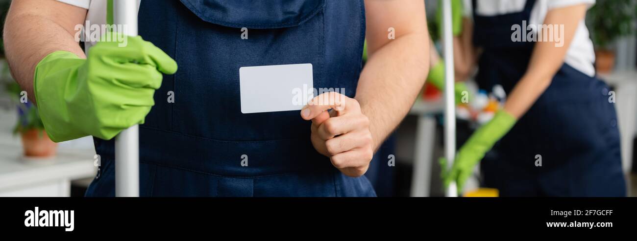 Cropped view of cleaner with mop holding empty card in office, banner ...