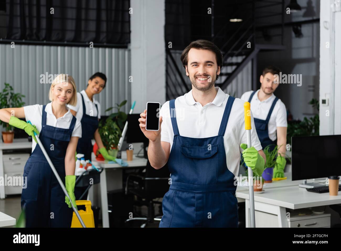 Smiling cleaner holding mop and cellphone with blank screen near ...