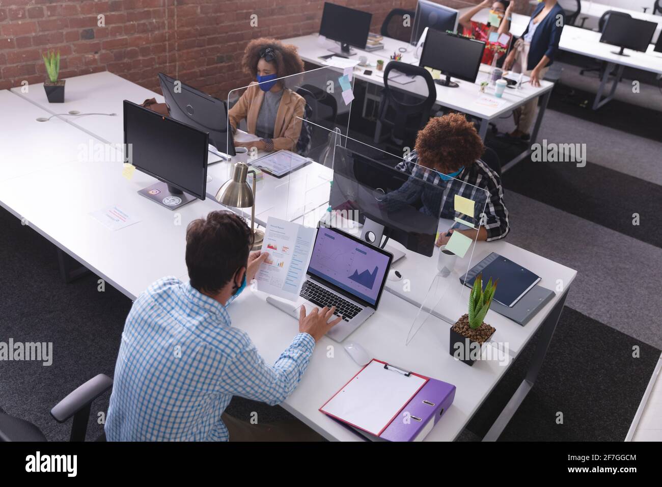Diverse group of creative colleagues wearing face masks using computers ...