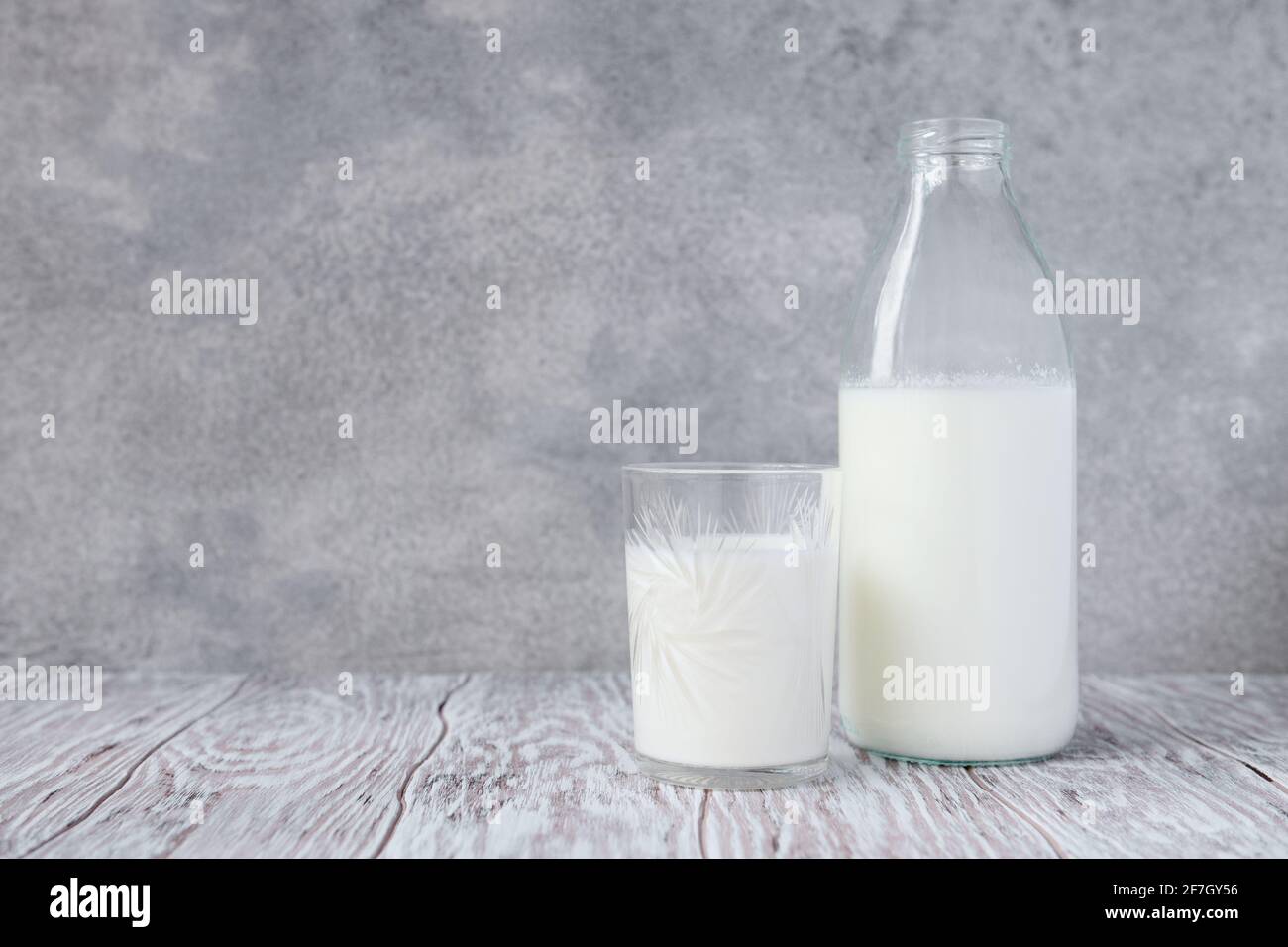 Glass beaker with milk and bottle of milk on a wooden table on a gray ...