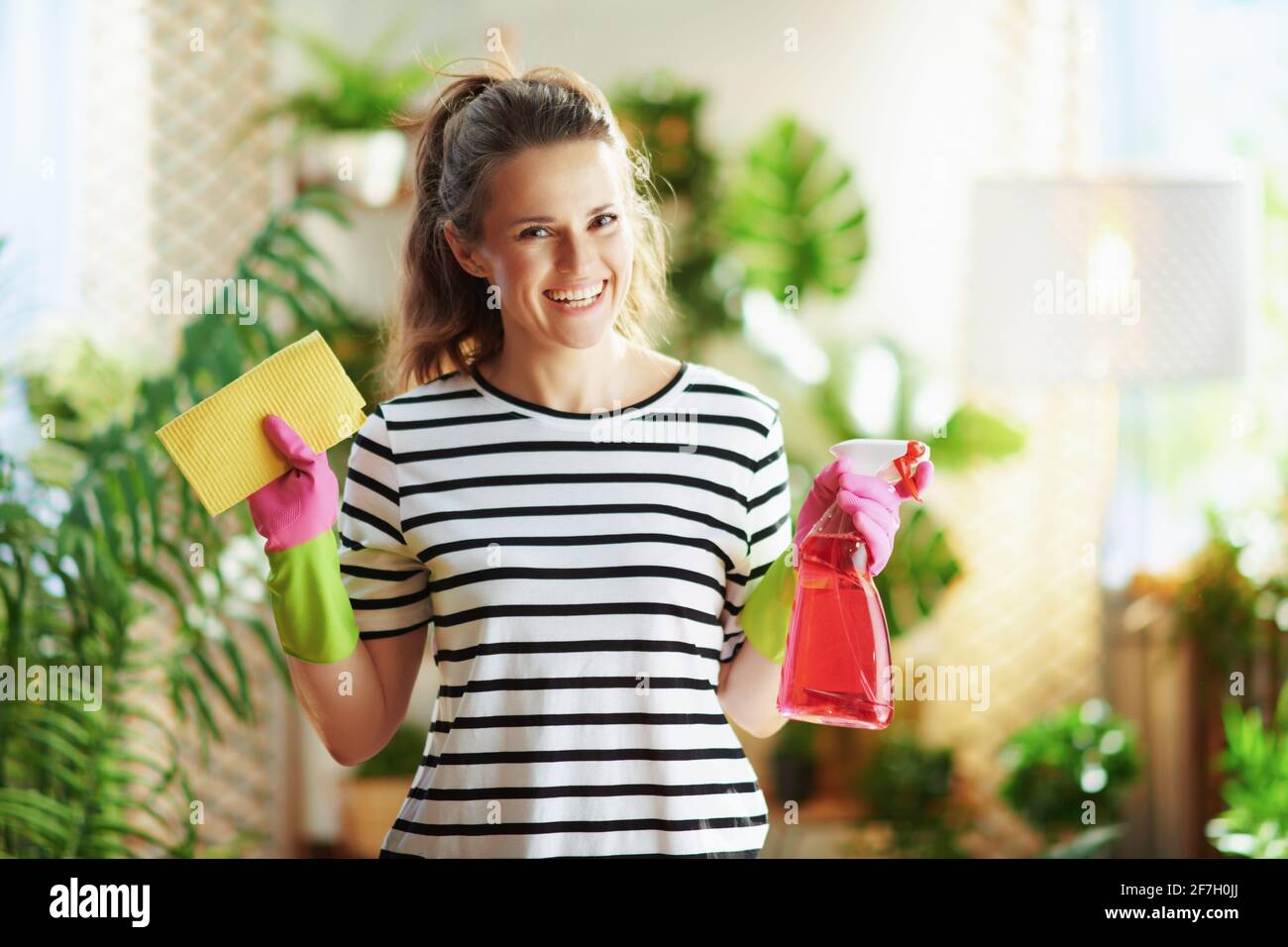 happy young woman in striped shirt with cleaning supplies doing ...