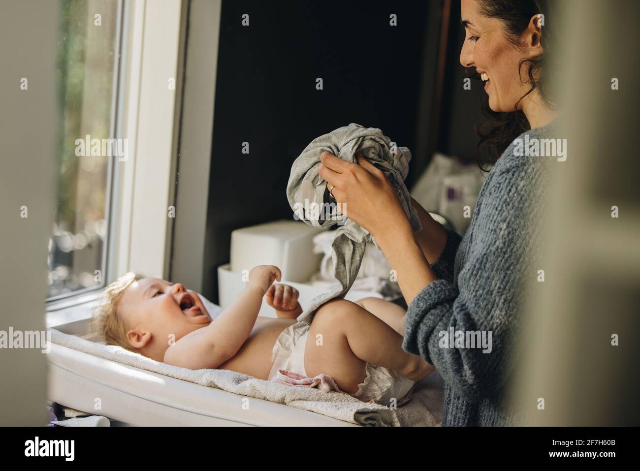 Mother changing baby's clothes and smiling. Mother getting her baby ...