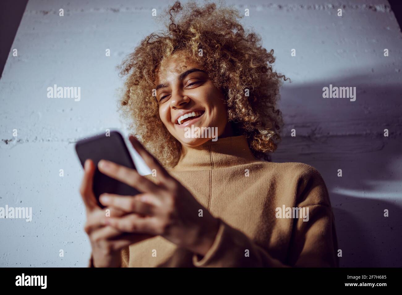 Cheerful mixed race rap girl standing against the pillar and using ...