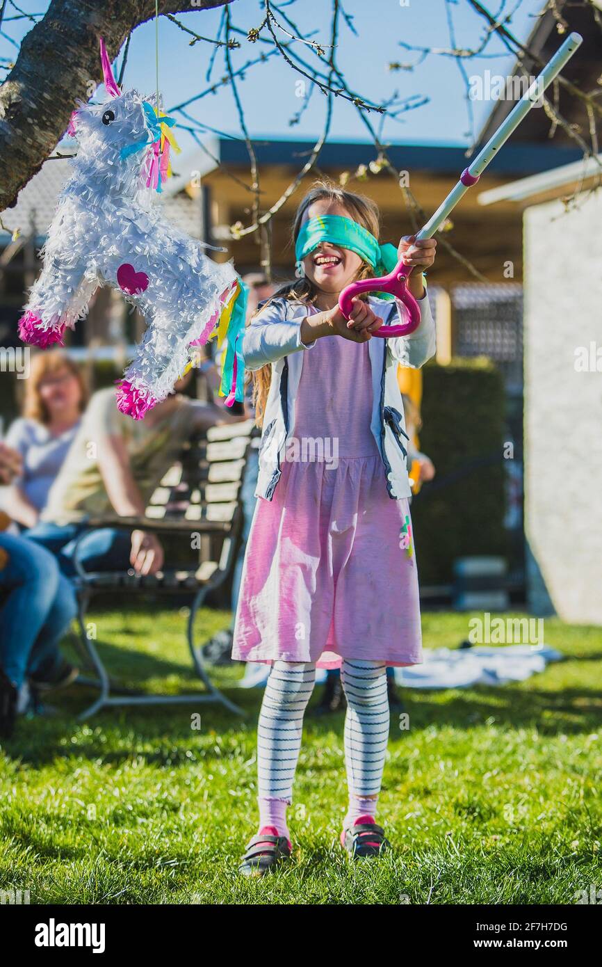 Young caucasian girl is hitting a white colored donkey shaped pinata ...