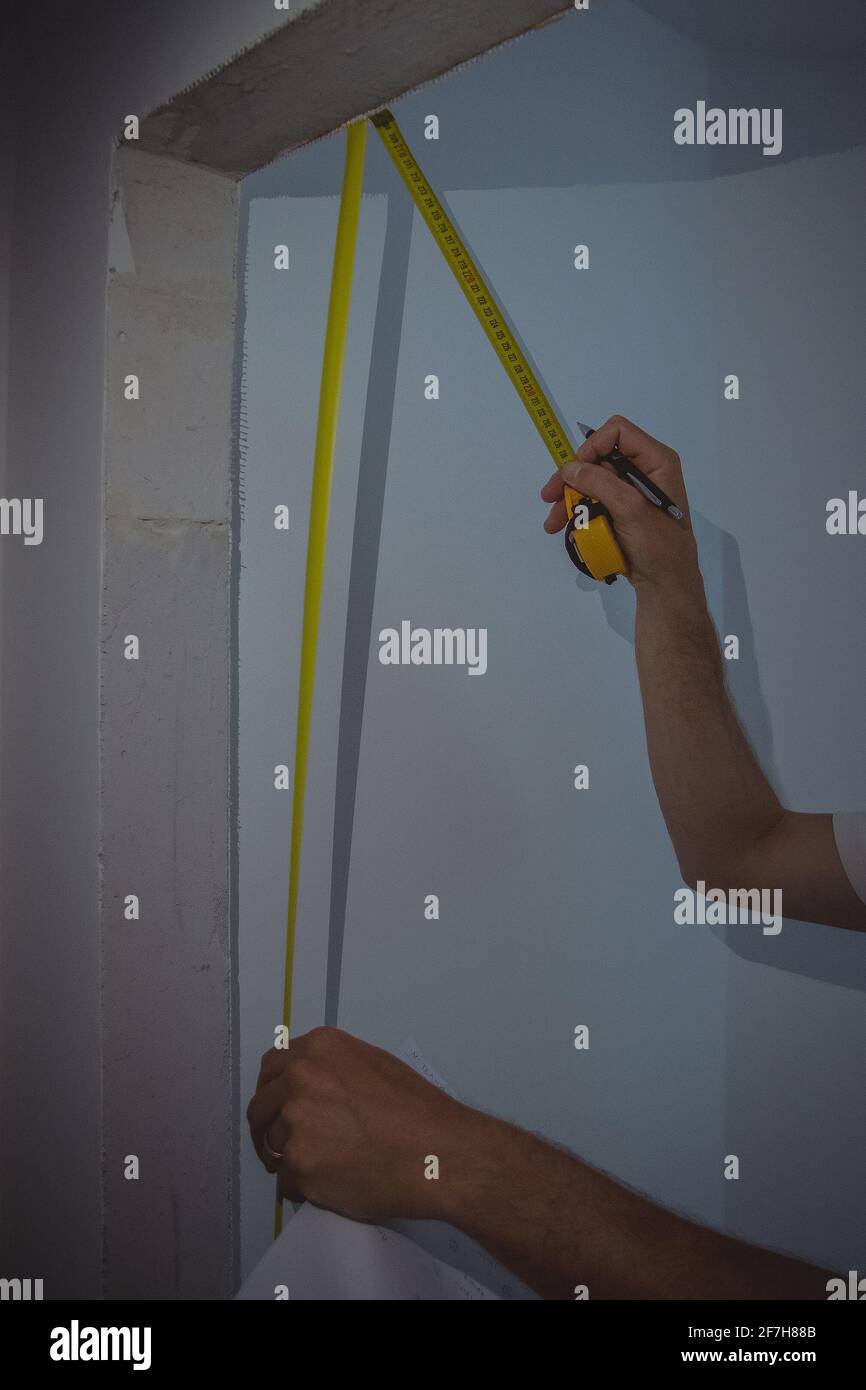 A person measuring width and height of a door opening with a yellow ...