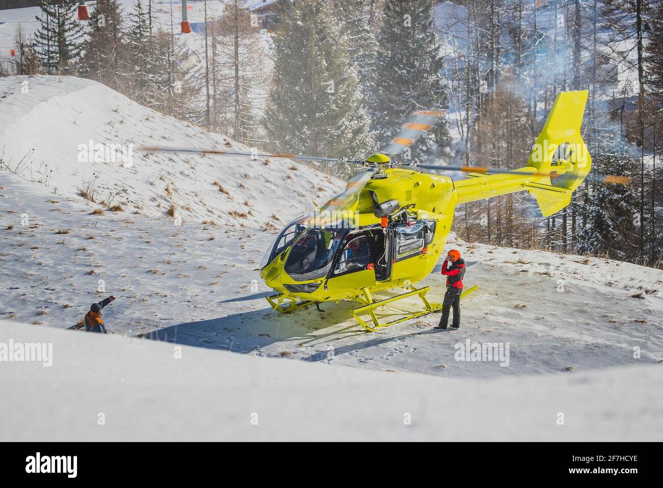 A yellow rescue helicopter is parked in the middle of the ski slope on ...