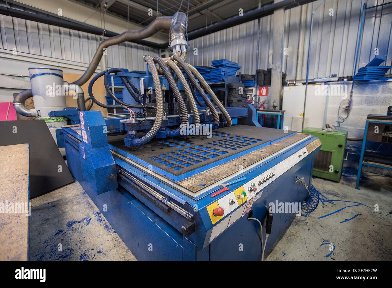 A big blue CNC machine is cutting holes on a foam material. Industrial ...