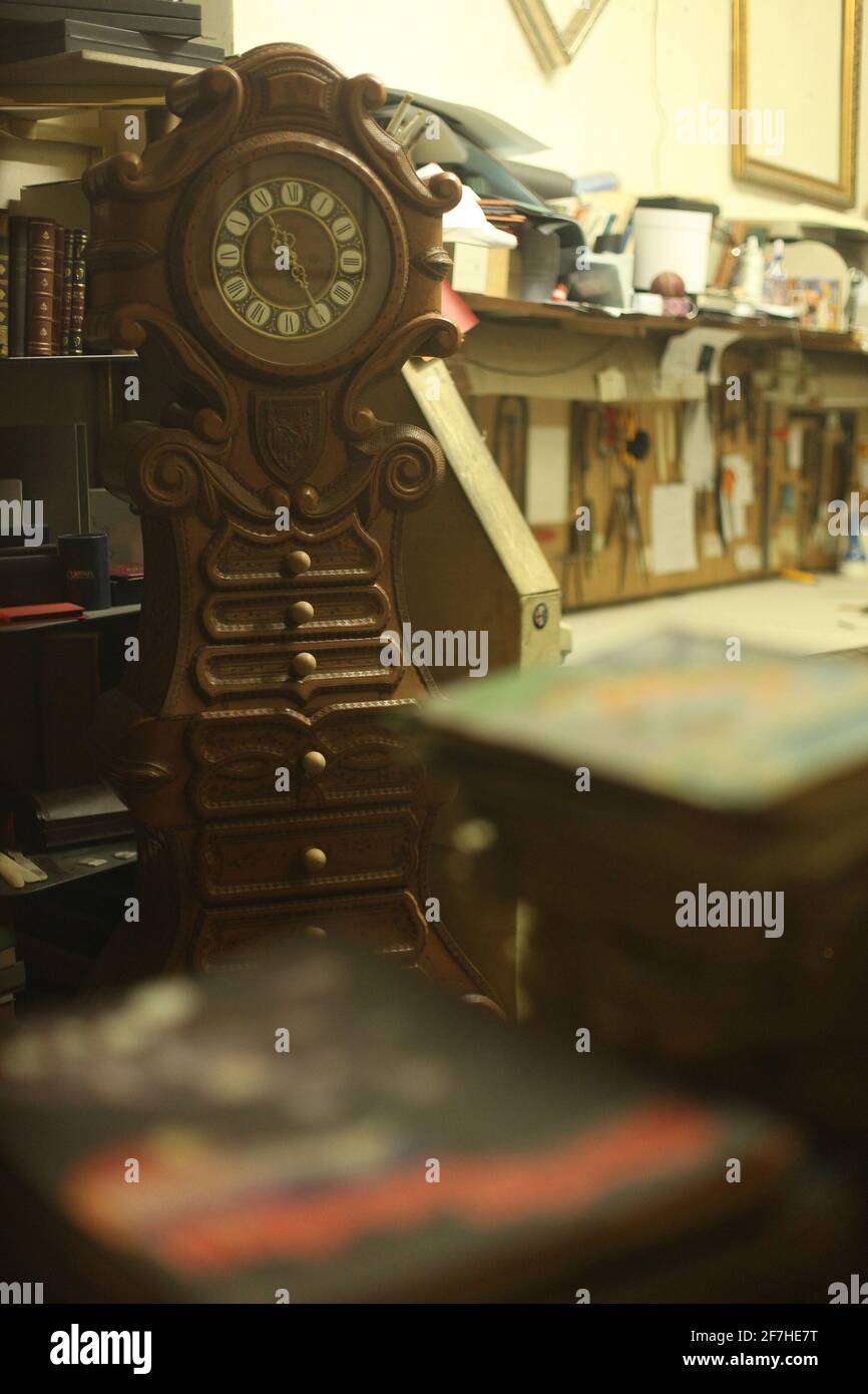 Old wooden clock in a workshop filled with tools, books frames and ...