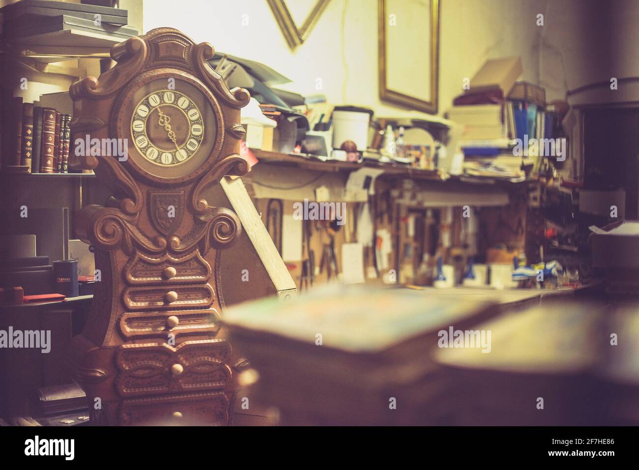 Old wooden clock in a workshop filled with tools, books frames and ...