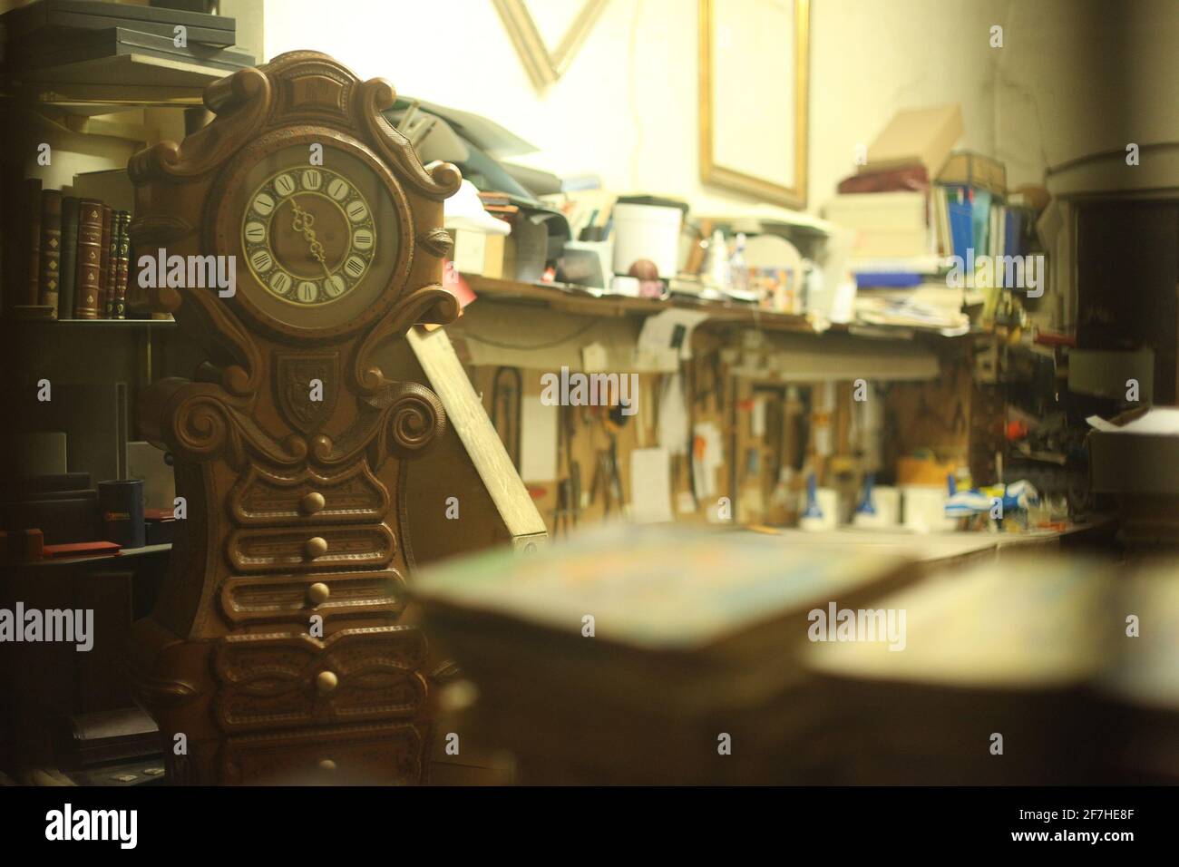 Old wooden clock in a workshop filled with tools, books frames and ...