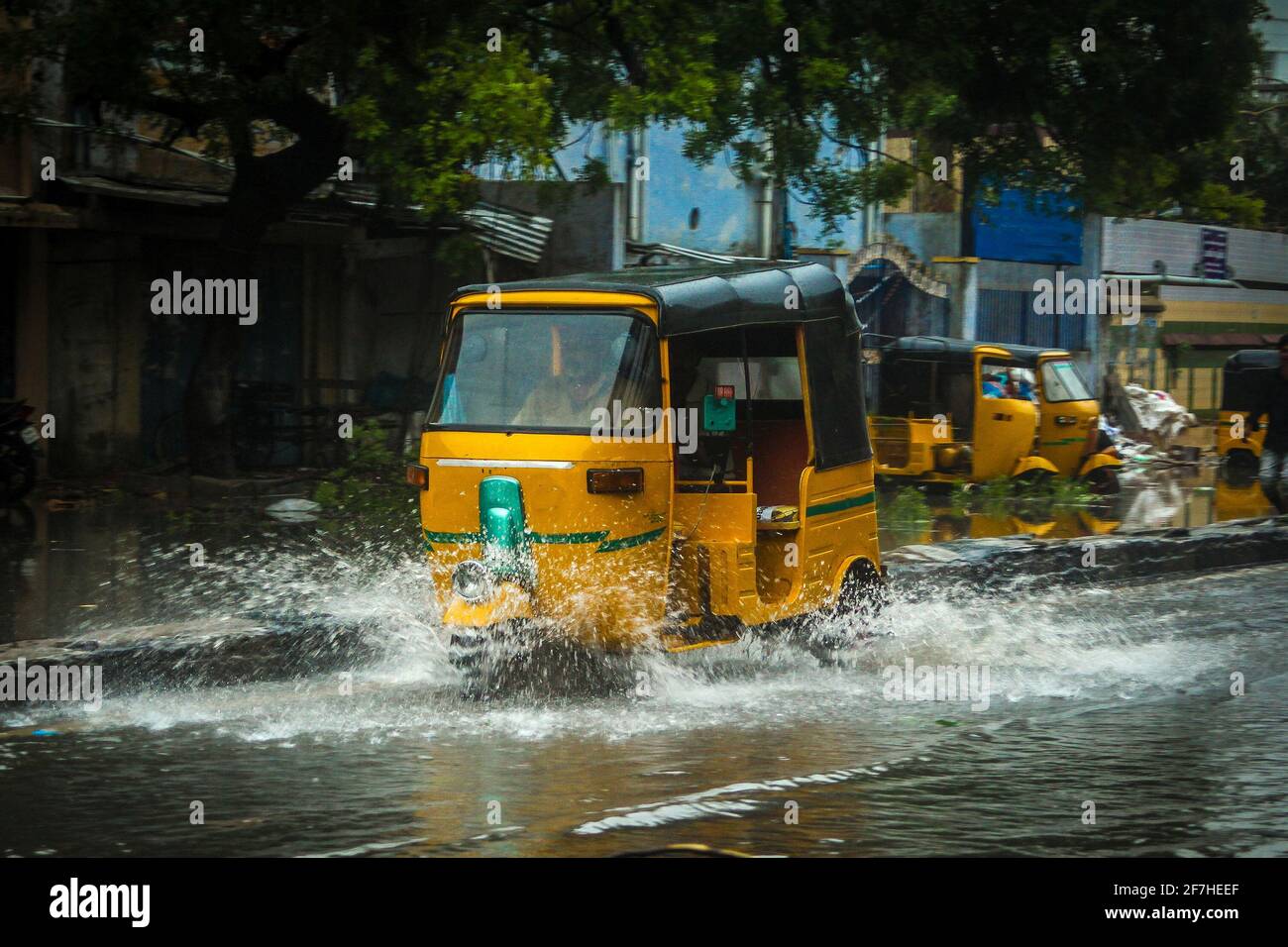 A yellow tuk-tuk in Chennai, India, is driving around on the flooded ...